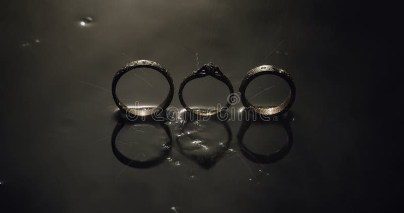 Wedding Rings and Engagement Ring Lying on Dark Water Surface Shining ...