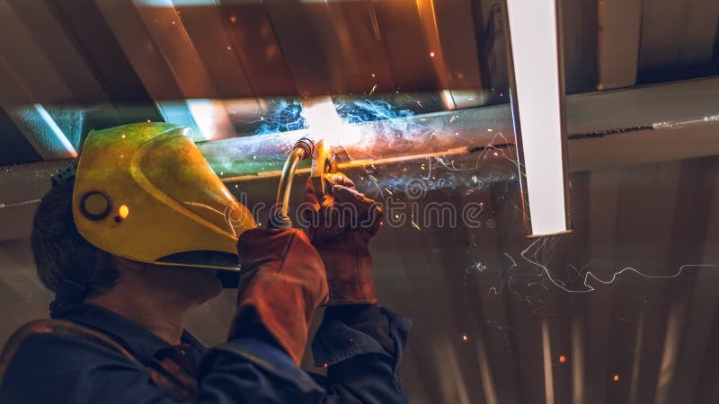 A Welder Wearing a Yellow Mask Performs the Work with a MIG-MAG Welding ...