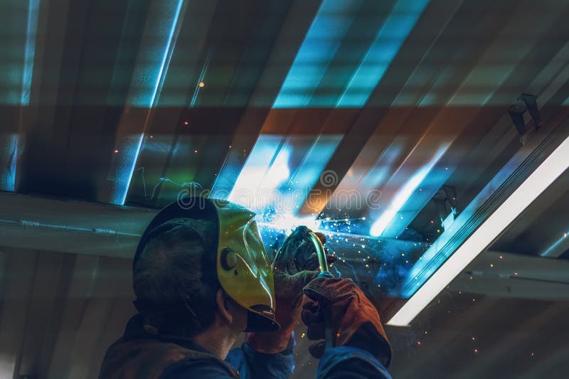 A Welder Wearing a Yellow Mask Performs the Work with a MIG-MAG Welding ...