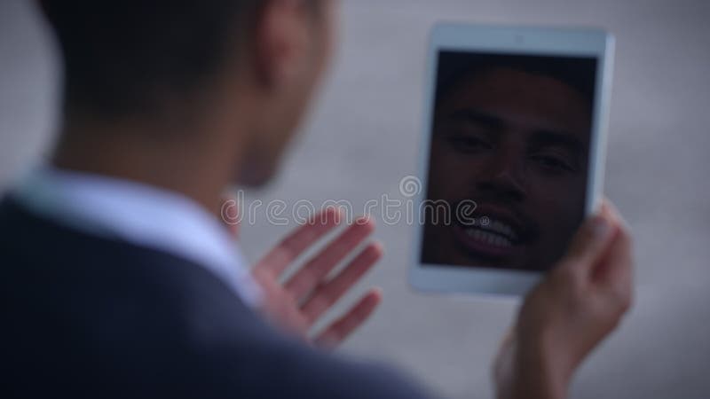 A Man is Smiling at the Reflection of Himself on a Tablet while in a ...