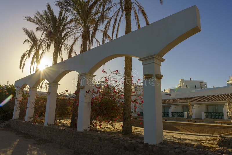 A White Archway with Four Pillars and a Row of Palm Trees in Front of a ...