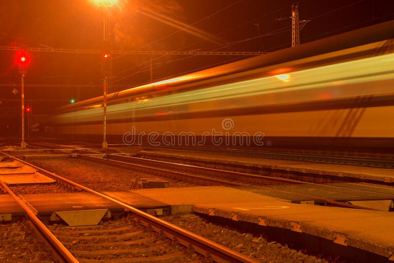 White and Blue Train Passing a Small Roofless Train Station at Night in ...