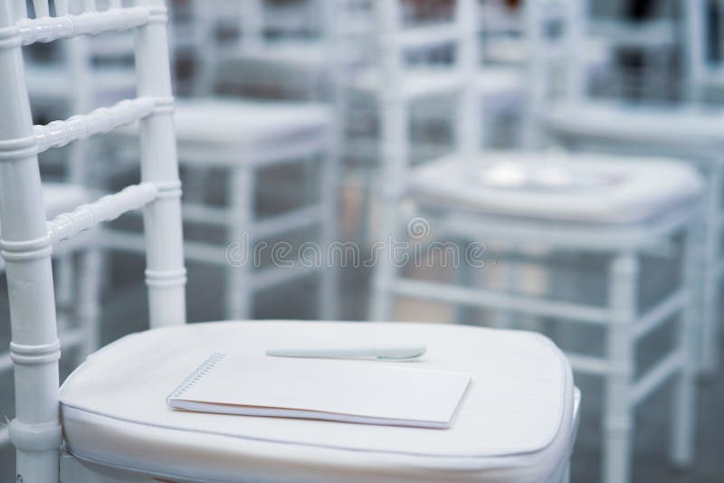 White Chairs in the Hall. There is a Notebook and a Pen on the Chair ...