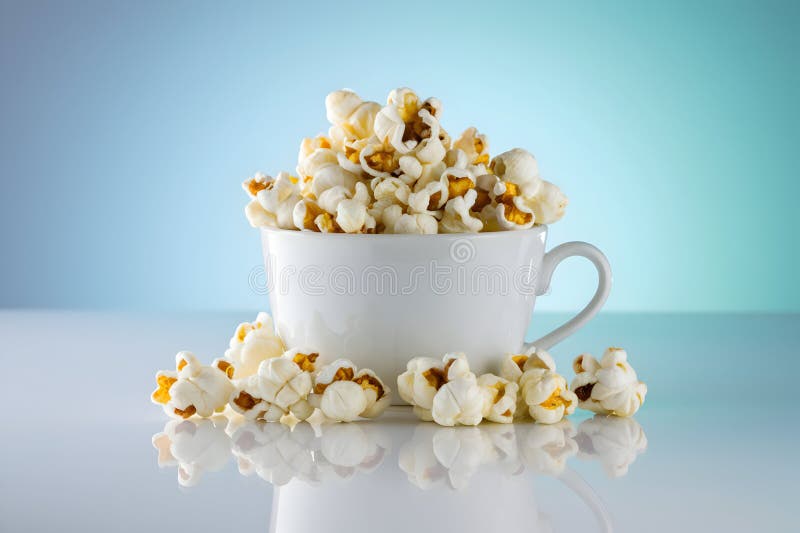 White Cup Filled with Golden Popcorn on a Reflective Surface Stock ...