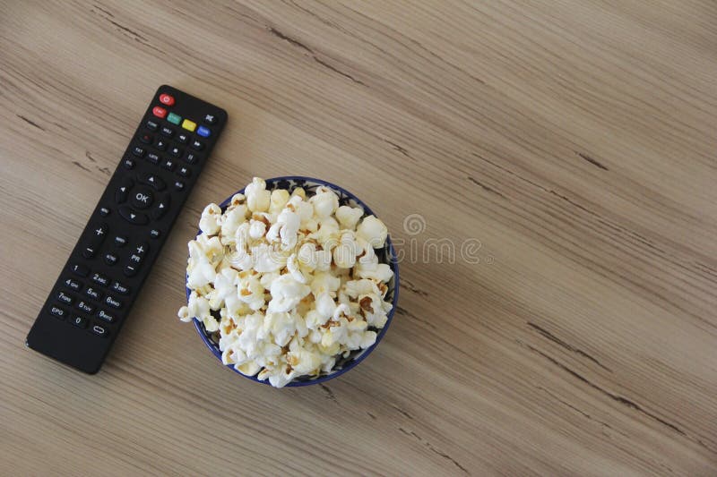 White Fried Popcorn and TV Remote Control on Brown Wooden Background ...