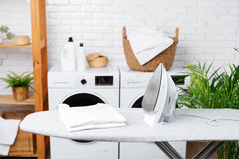 White Iron on Grey Ironing Board Next To Laundry Machines in White Room ...