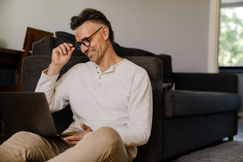 White Man Smiling and Using Laptop while Sitting on Floor at Home Stock ...