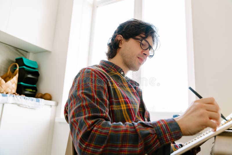 White Man Wearing Glasses Writing Down Notes while Sitting in Kitchen ...