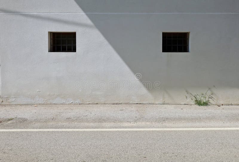 White Plaster Facade with Two Barred Windows at the Roadside. Shadow ...