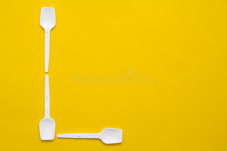 White Plastic Spoons in the Form of Letter L on Yellow Background. Top ...