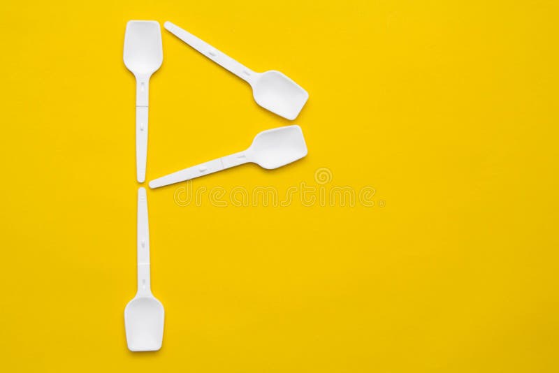White Plastic Spoons in the Form of Letter P on Yellow Background. Top ...