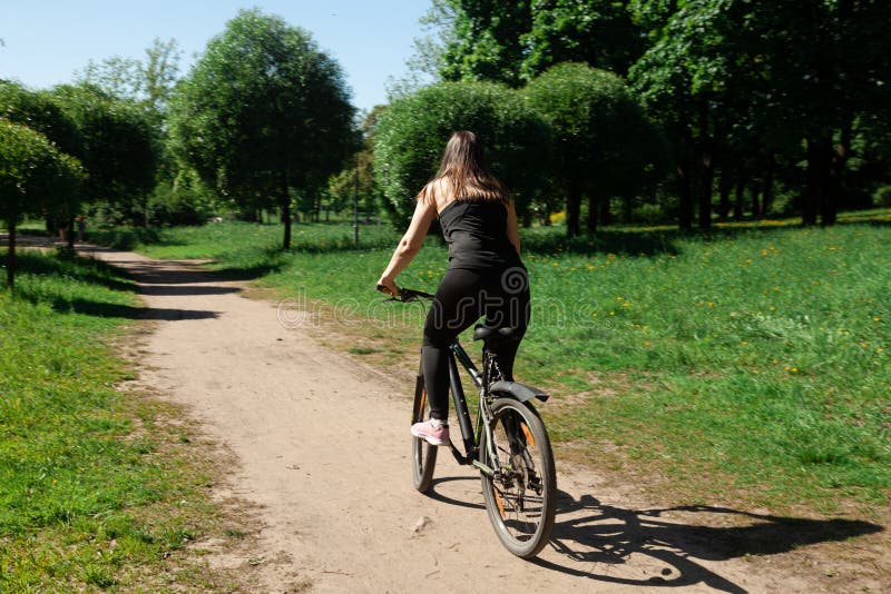 A White-skinned Girl Rides a Bicycle through a Summer Park. View from ...