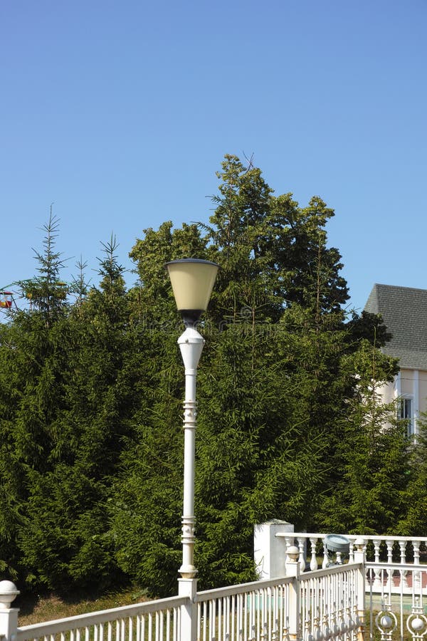 White Street Lamp on a Railing in Front of a Line of Trees Stock Image ...