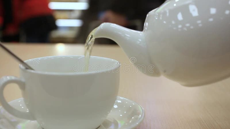 White Teapot Pouring Tea into Cup in Slow Motion. Cafe Interior ...