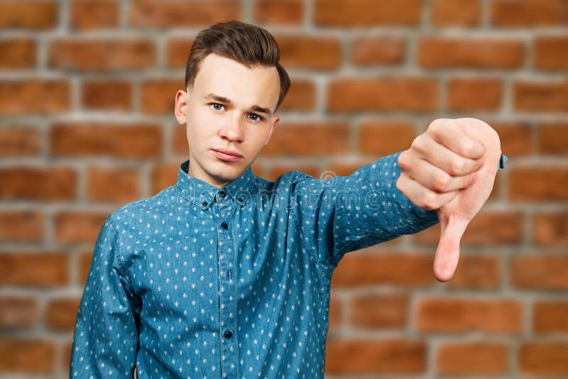 White Young Man Dressed in Blue Shirt Showing Thumbs Down on Brick Wall ...