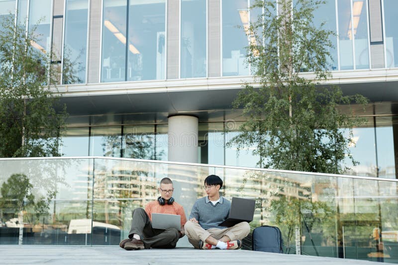 Two Man Working Together on Laptops Sitting on Pavement Outdoors Stock ...