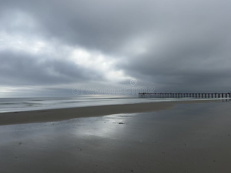 Wide Wet Desolate Beach with Storm Clouds and a Long Pier Going Out ...