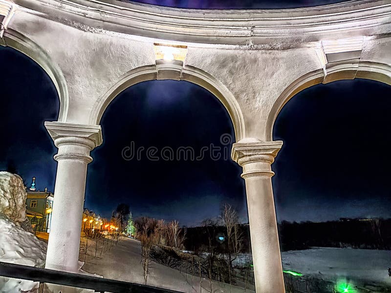 Winter Night View through an Arched Stone Balcony Overlooking a Lit ...
