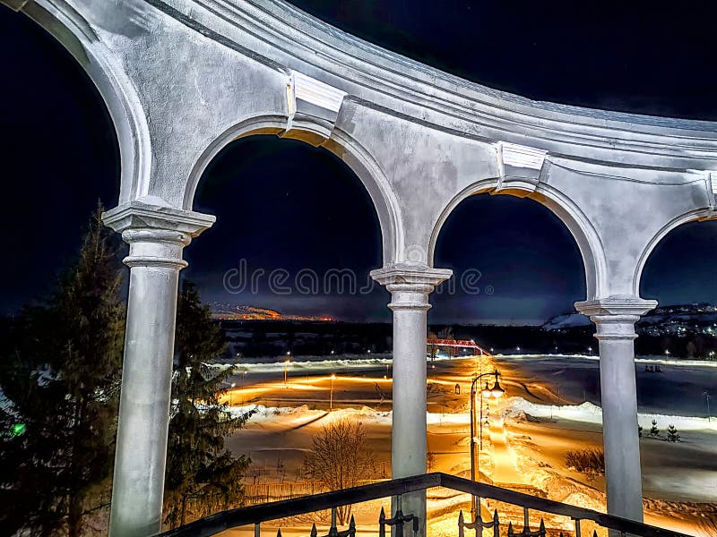 Winter Night View through an Arched Stone Balcony Overlooking a Lit ...