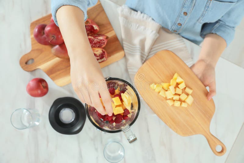 Woman Adding Mango into Blender with Ingredients for Smoothie at Table ...