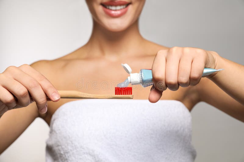 Woman Applying Toothpaste On Brush Against Light Background Closeup