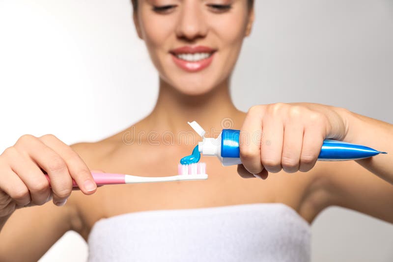 Woman Applying Toothpaste On Brush Against Light Background Closeup