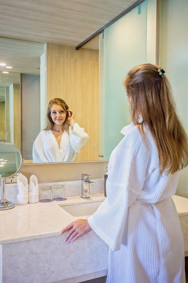 Woman In Bathrobe Applying Facial Cream On Healthy Skin In The Bathroom