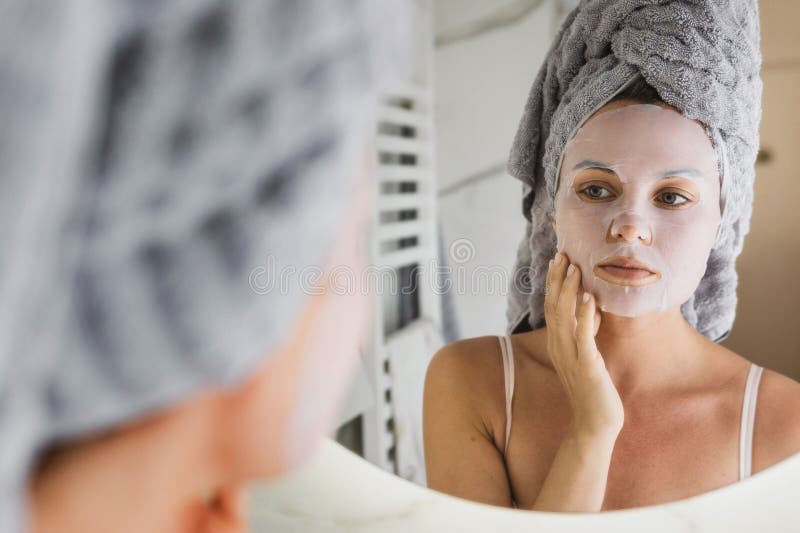 Woman in Bathroom with Applied Sheet Mask on Her Face Looking in the ...