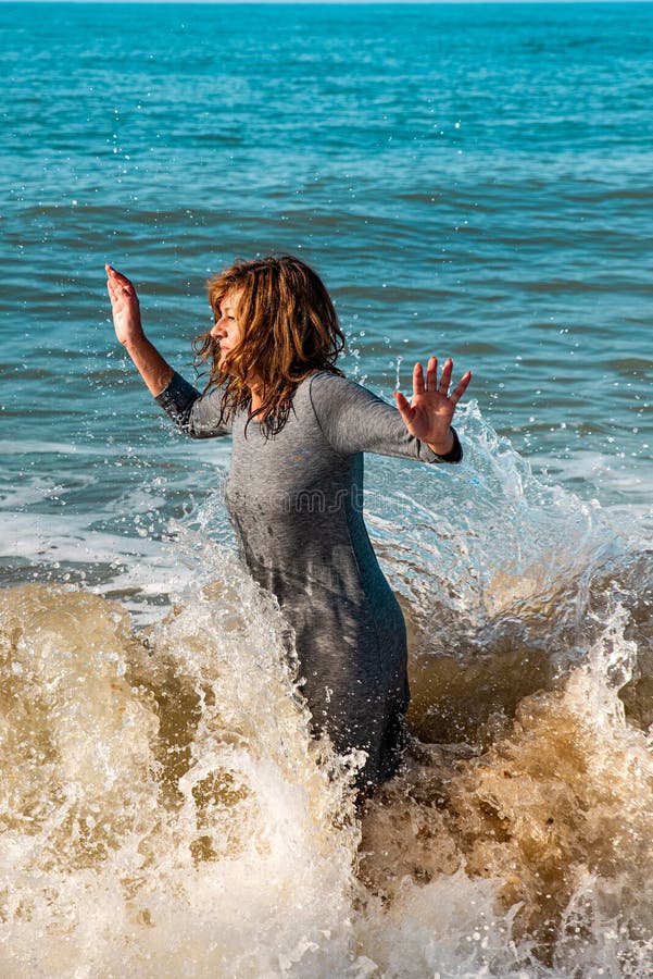 Woman Jumping a Wave on the Beach in a White Shirt and Jean Shorts ...