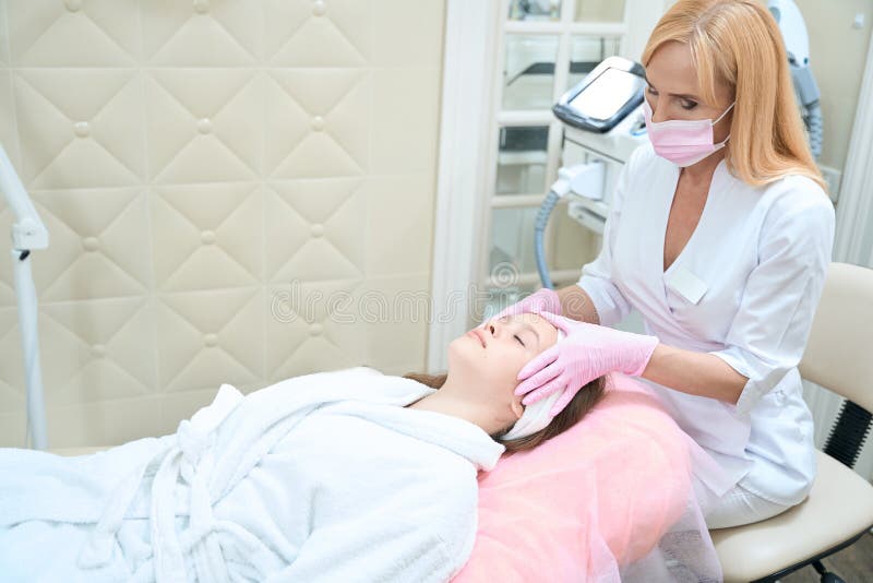 Woman Beautician Makes Face Massage To Girl In Beautician Office Stock