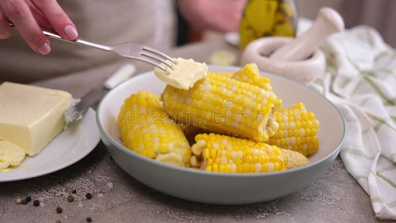Woman Buttering Freshly Cooked Corn in Ceramic Plate on a Kitchen Table ...