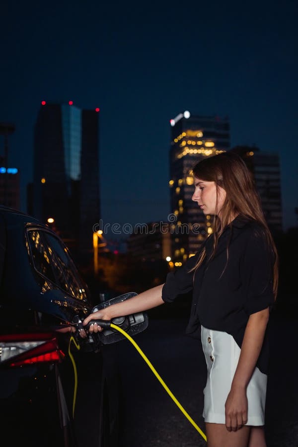Woman Charging an EV Car in City at Night Stock Photo - Image of ...