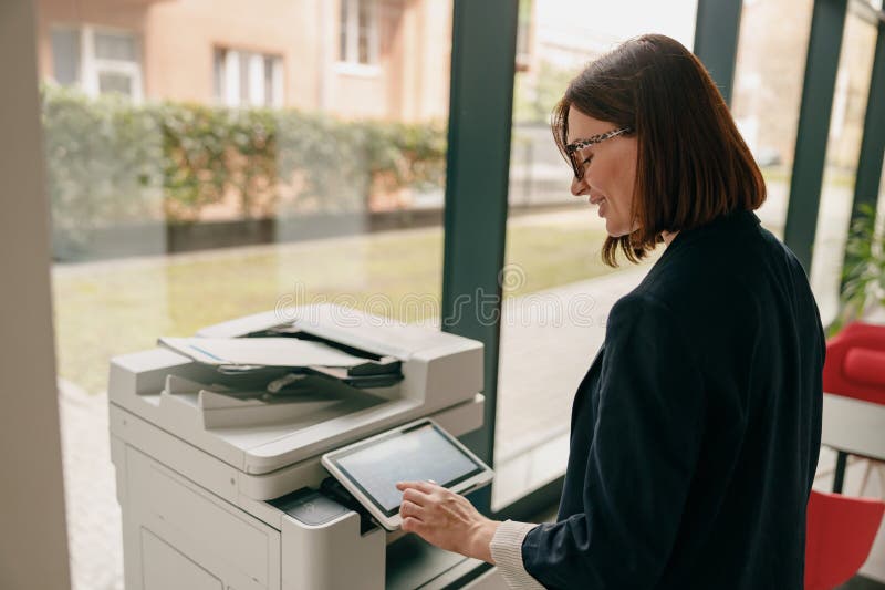 A Woman is Using a Copier in a Modern Office with Glass Windows for ...