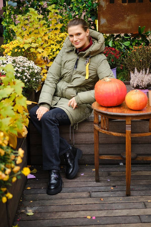 Woman in Down Jacket Sits on Bench Surrounded with Autumn Flowers Stock ...