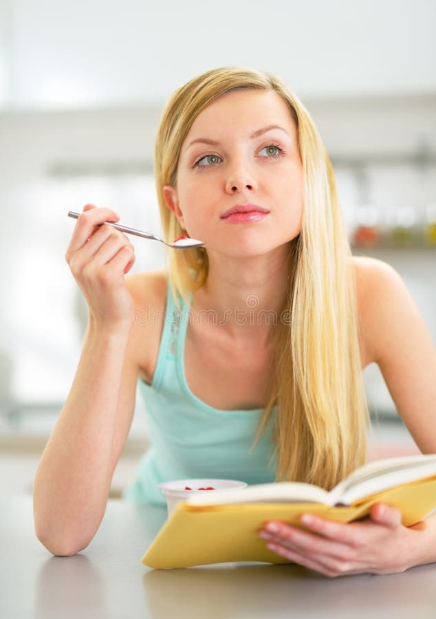 Woman Eating Yogurt in Kitchen and Reading Book Stock Photo - Image of ...