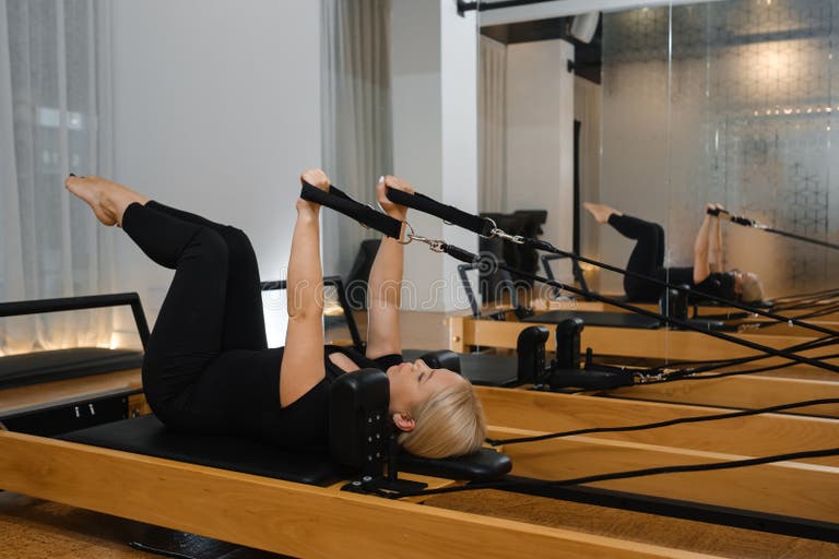 Woman Practicing Pilates on Reformer Equipment in a Bright Studio with ...