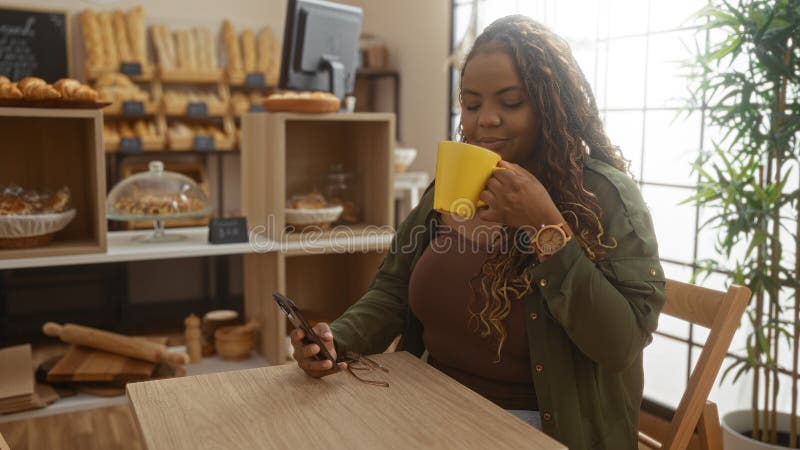 Woman Enjoying Coffee while Scrolling on Phone in a Cozy Bakery with ...