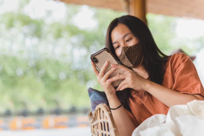 Woman in Face Mask Using Her Mobile Phone while Sitting in a Chair ...