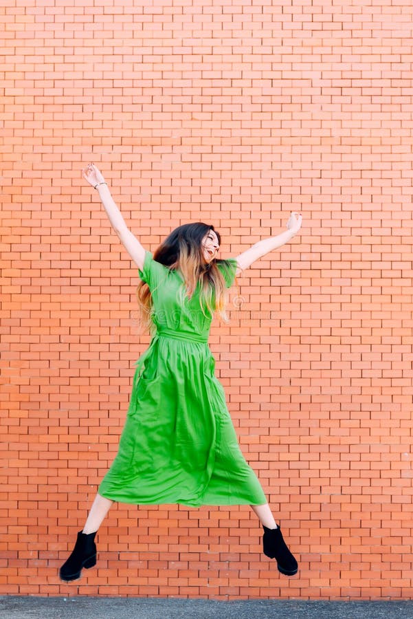 Woman in a Green Dress Jumping Up and Down Happily in Front of a Brick ...
