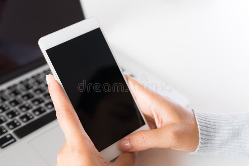 Woman Hand Holding White Mobile Phone on a Table with a Laptop Stock ...
