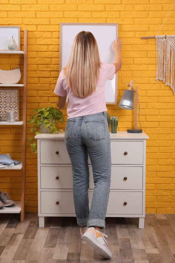 Woman Hanging Frame on Yellow Brick Wall Indoors, Back View Stock Image ...