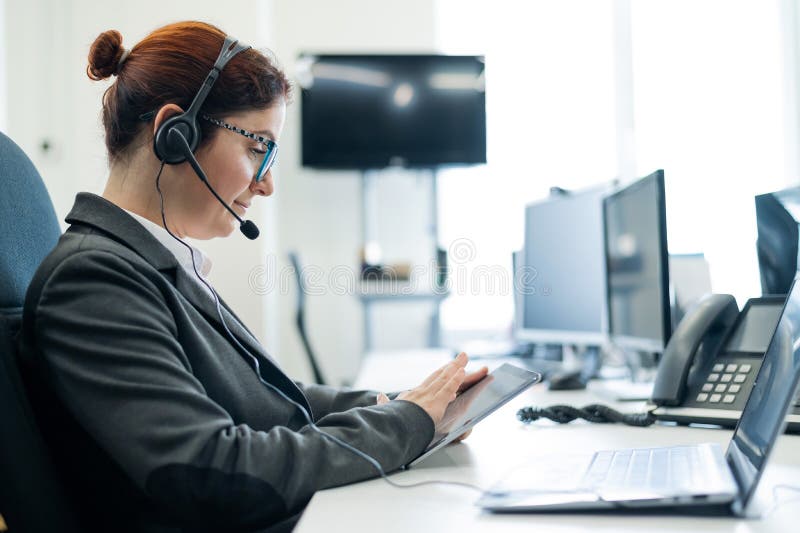 Woman in Headset Sits at Her Desk in the Office and Uses Digital Tablet ...