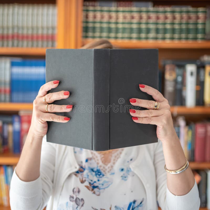 Woman Holding an Open Book that Covers Her Face with a Large Bookcase ...
