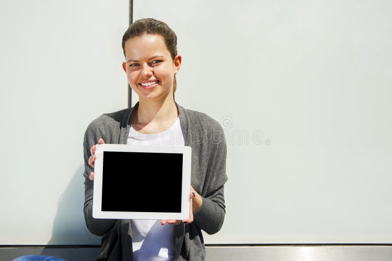Woman Holding a Tablet Computer Over Glass Wall Smiling Over White Wall ...