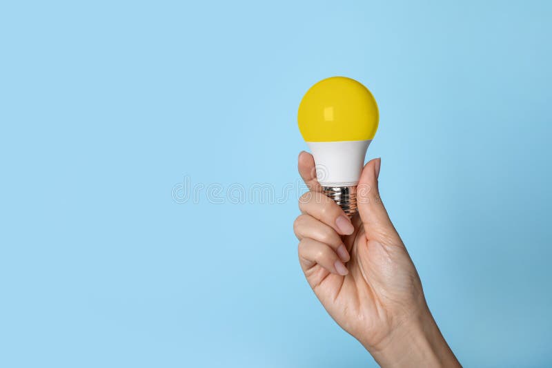 Woman Holding Yellow Bulb on Light Blue Background, Closeup. Space for ...