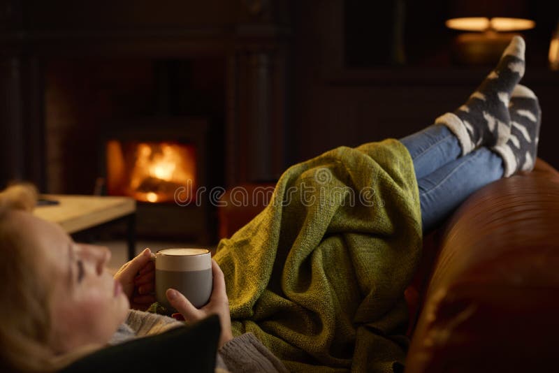Woman at Home in Lounge Lying on Sofa with Cosy Fire with Hot Drink ...