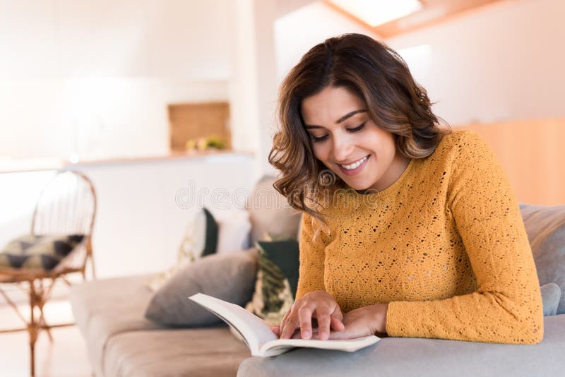 Woman reading book on sofa stock photo. Image of apartment - 170607750