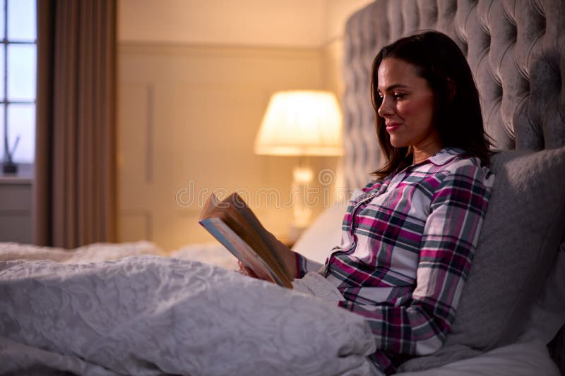 Woman at Home Sitting in Bed in Evening Reading Book Stock Photo ...