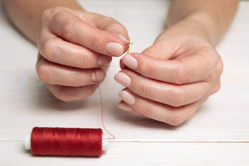 A Woman Inserts a Red Thread into a Needle. Stock Image - Image of ...
