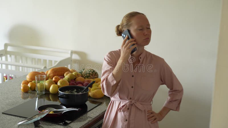 A Woman in the Kitchen Multitasks by Talking on a Cell Phone while ...
